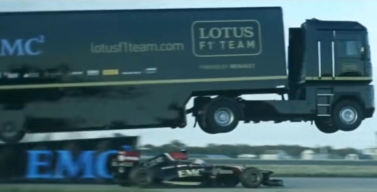 A Semi-Truck With Attached Trailer Jumps Over a Speeding Formula 1 Race Car